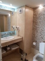 Casa de banho com lavatório, espelho, porta-toalhas, sanita e um contentor de lixo.
