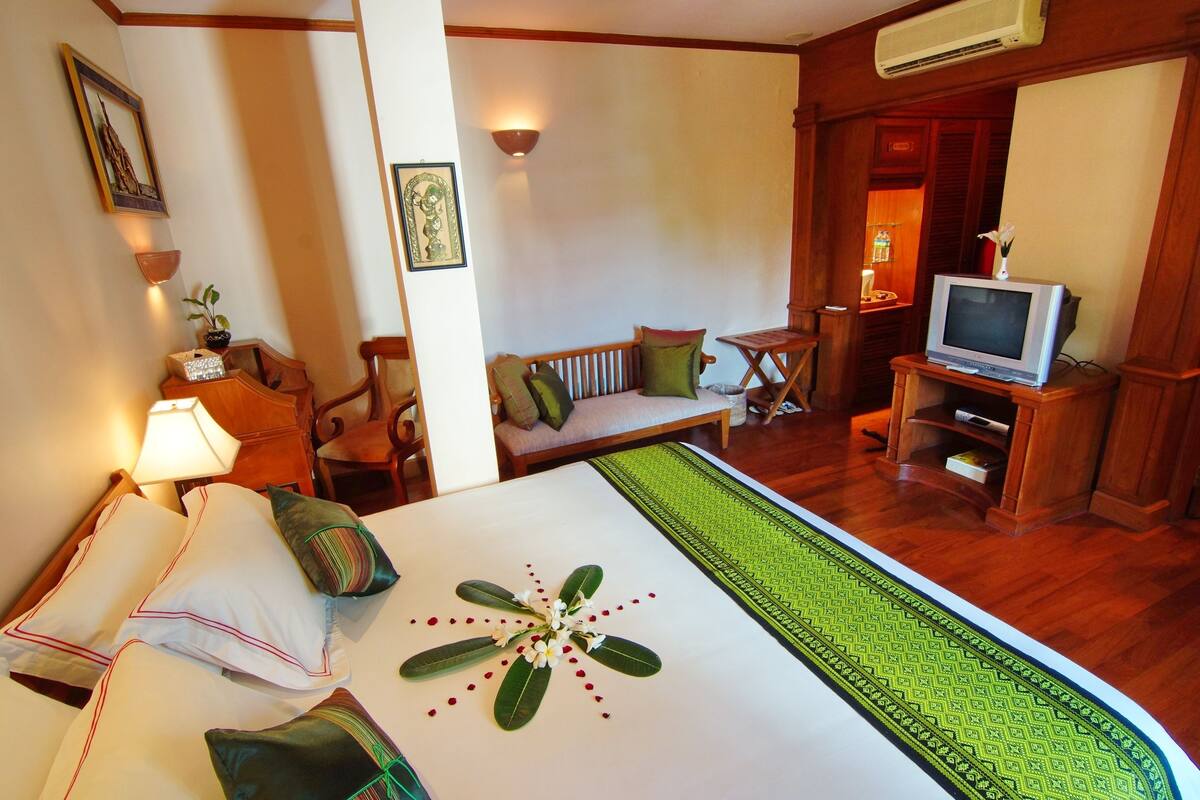 Quarto de hotel com cama, televisão em móvel, sofá, poltrona e pequena mesa.