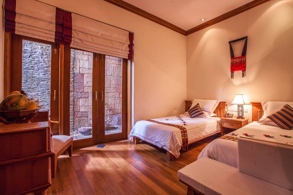 Quarto de hotel com duas camas, piso de madeira, parede de pedra e uma grande janela com vista.