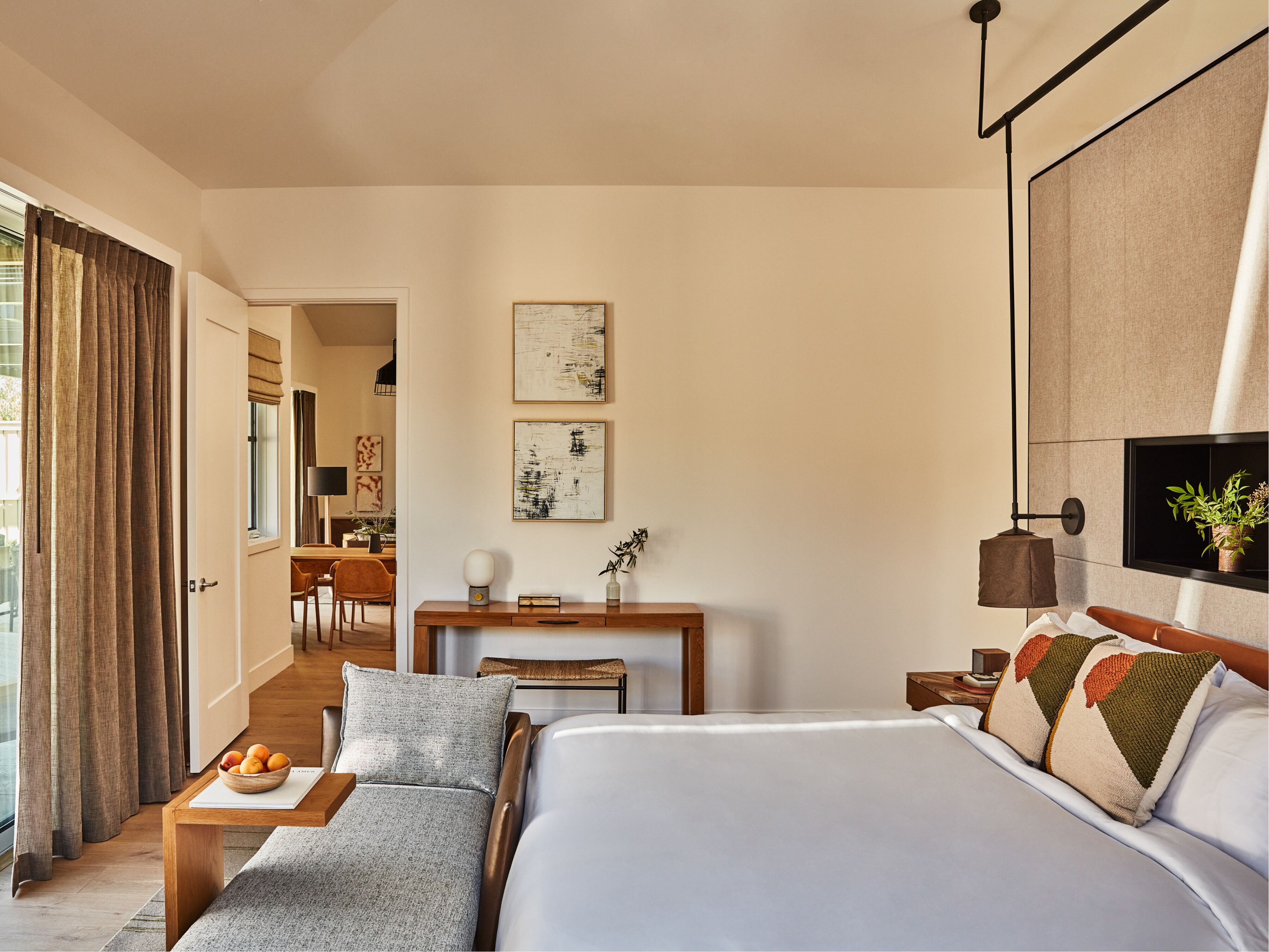 Quarto de hotel moderno com uma cama grande, uma escrivaninha com cadeira, uma mesinha com frutas e vista para o exterior.
