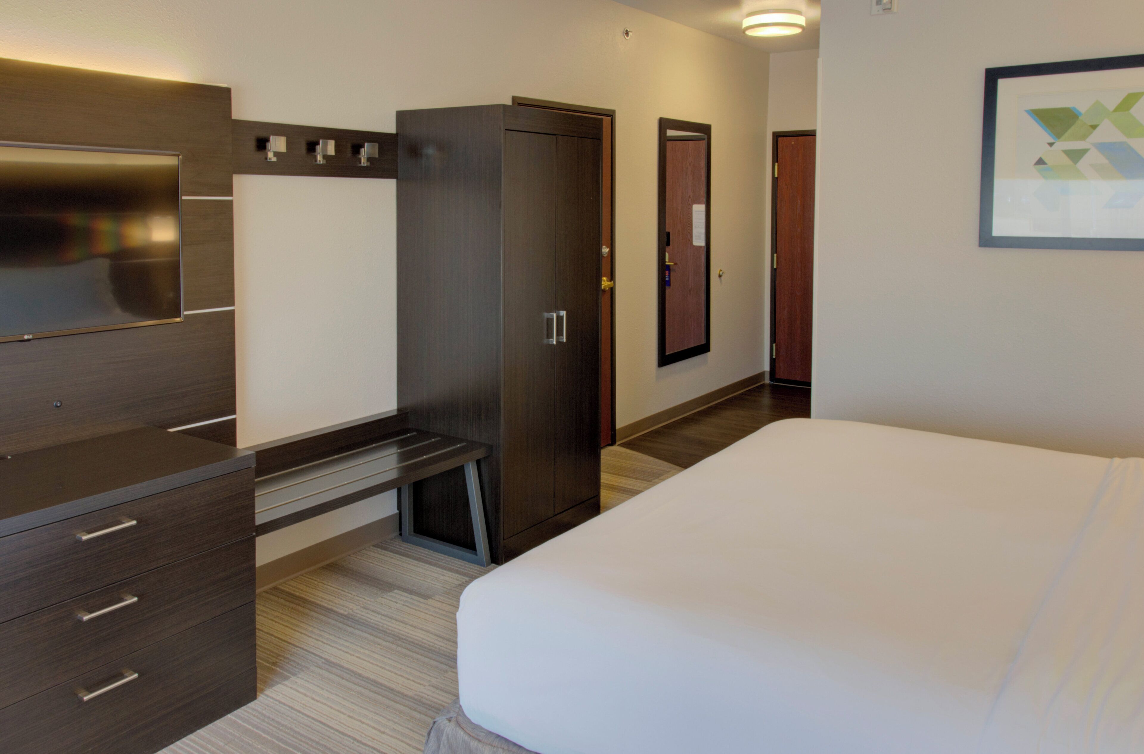 Quarto de hotel com cama, escrivaninha, guarda-roupa e televisão.