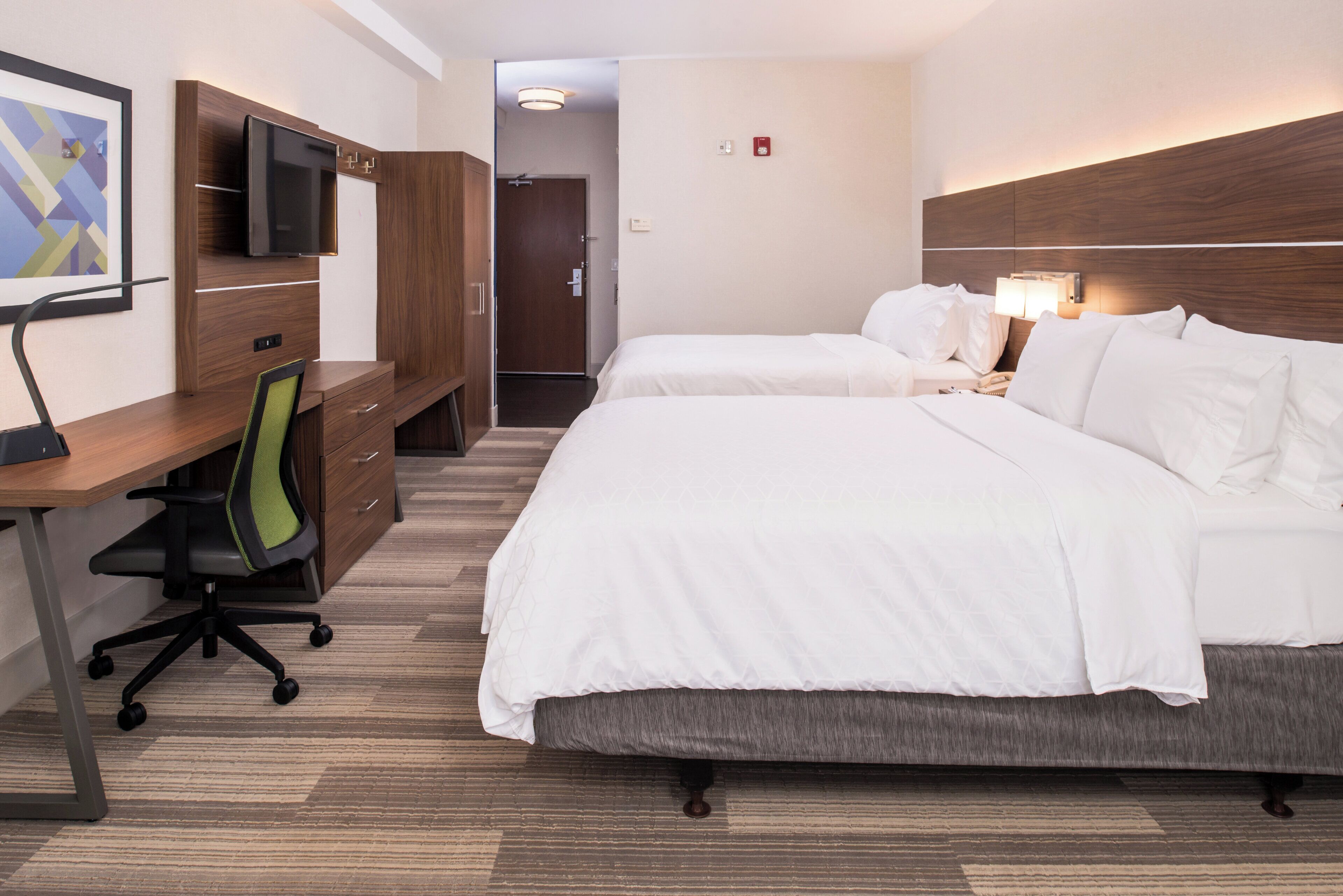 Quarto de hotel com uma mesa, duas camas, televisão e porta que dá para outro aposento.