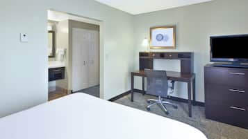 Quarto de hotel com cama, escrivaninha, cadeira, televisão e guarda-roupa.