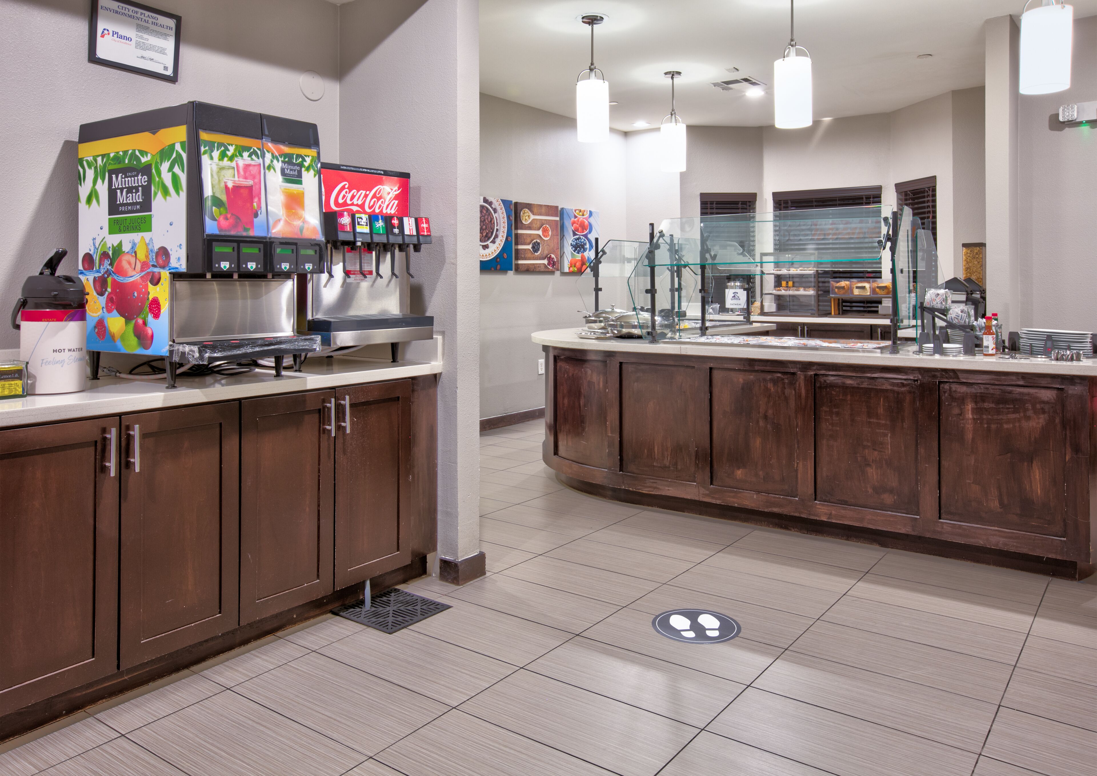 Um saguão de hotel com um posto de bebidas de serviço e uma máquina de café, além de um balcão com opções de comida.