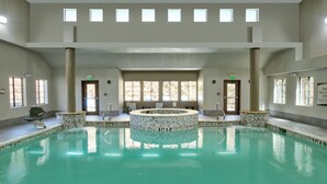 Uma grande piscina interior com hidromassagem, várias janelas e chão revestido de azulejos.