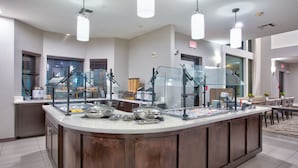 Uma área de buffet com ilha central, vitrines de vidro e iluminação pendente.