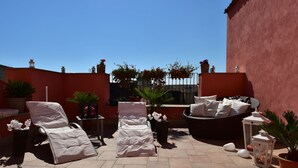 Um terraço ao ar livre com duas poltronas, um sofá e plantas em vasos.