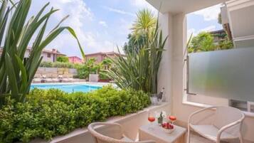 Varanda com móveis de vime, piscina e plantas tropicais.
