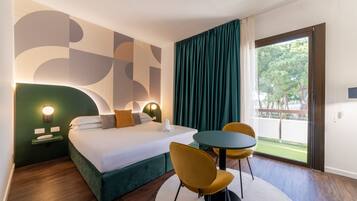 Quarto de hotel moderno com uma cama grande, duas cadeiras, uma mesa pequena e vista para o exterior.