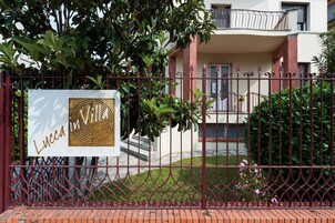Placa com o nome 'Bed & Breakfast Lucca', mostrando um edifício e uma vedação metálica vermelha.
