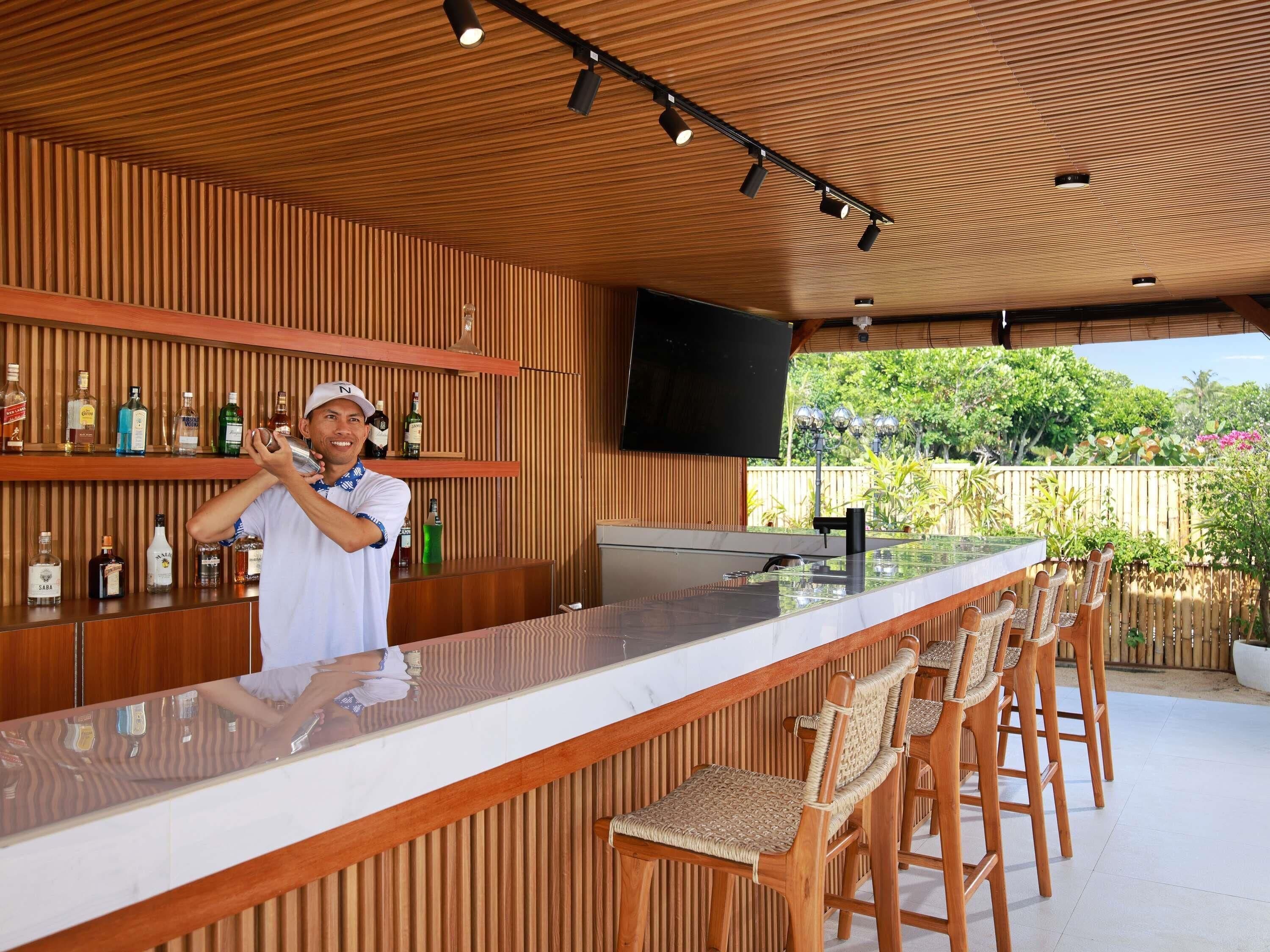 Uma área de bar com painéis de madeira, um balcão comprido e várias cadeiras de vime.