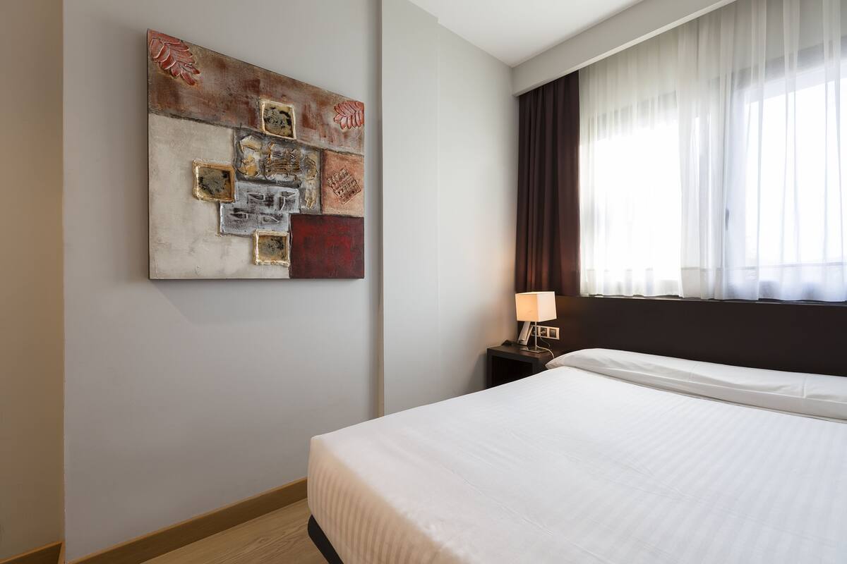 Quarto de hotel com uma cama grande, uma mesa de cabeceira com abajur e uma obra de arte na parede.