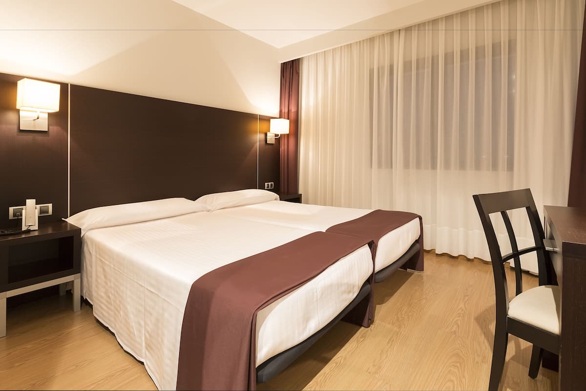 Quarto de hotel com uma cama grande, mesas de cabeceira, escrivaninha e uma cadeira.