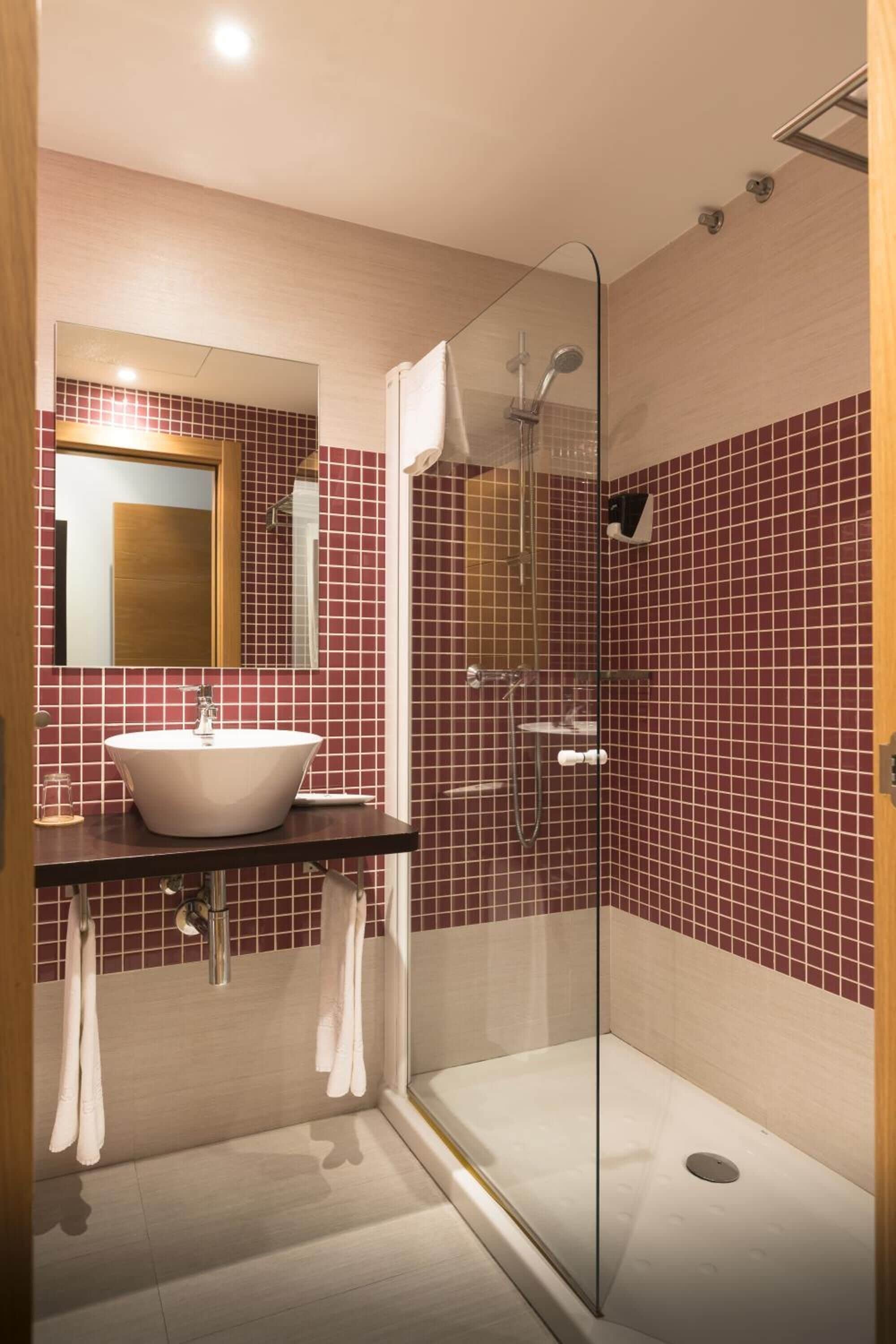 Uma casa de banho moderna com cabine de duche em vidro, lavatório com espelho e paredes com azulejos vermelhos.
