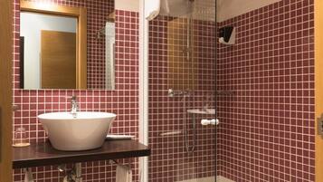 Uma casa de banho moderna com cabine de duche em vidro, lavatório com espelho e paredes com azulejos vermelhos.
