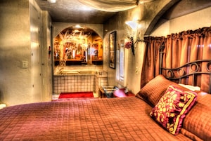 Quarto com uma cama grande, banheiro com banheira e espelho refletindo o ambiente.