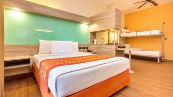 Quarto de hotel com cama, beliche, ventilador de teto e banheiro com espelho e pia.