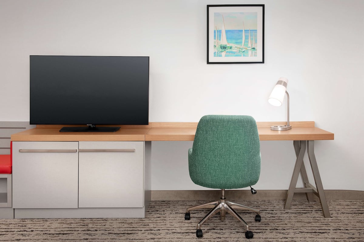 Uma mesa de escritório moderna com uma televisão de tela plana, uma cadeira de escritório verde e uma luminária de mesa.