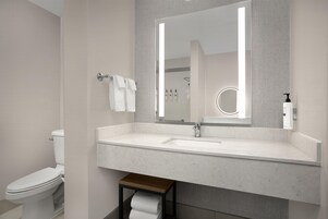 Uma casa de banho moderna com uma sanita, um lavatório branco e um espelho.