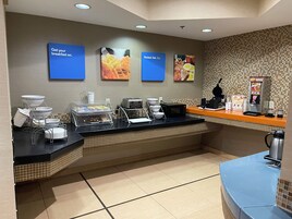 Espaço de café da manhã com estação de autoatendimento, incluindo máquina de café, torradeira e diversos recipientes para alimentos.