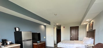 Quarto de hotel com cozinha compacta, cama, escrivaninha e guarda-roupa.