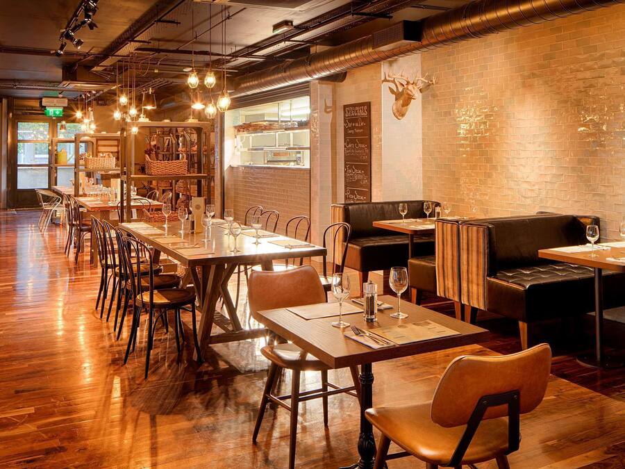 Um restaurante com mesas e cadeiras de madeira, parede de tijolos e luminárias pendentes.