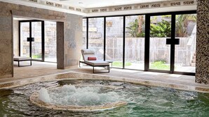 Uma área de spa com hidromassagem, uma espreguiçadeira e vista para o exterior por grandes janelas.
