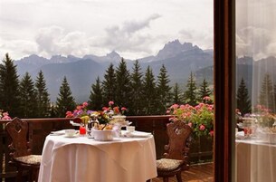 Área de refeições ao ar livre com uma mesa posta para dois, com vista para uma paisagem montanhosa.