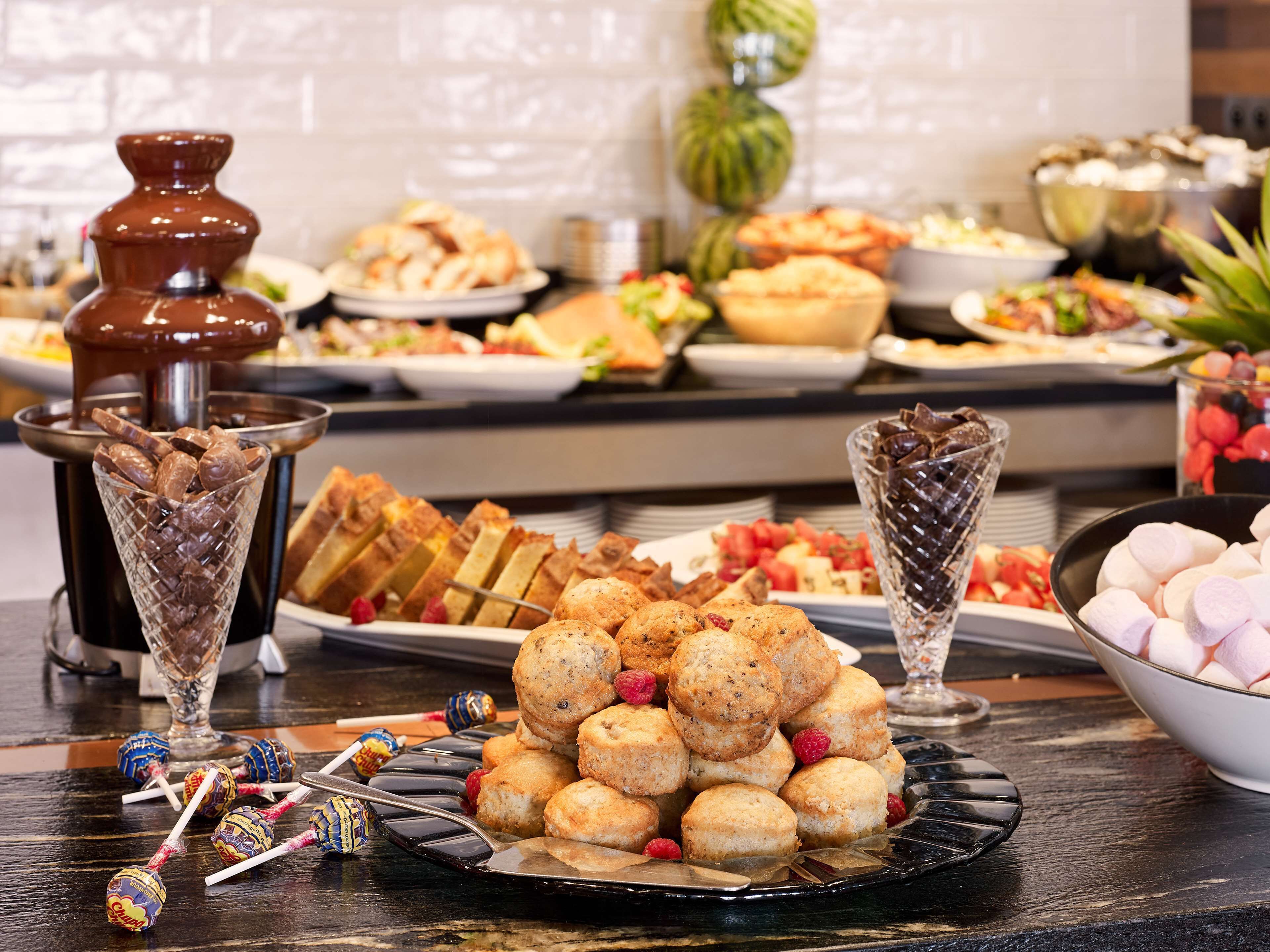 Uma mesa de buffet com diversos alimentos, incluindo chocolate, bolinhos e pirulitos.