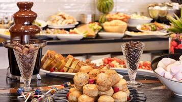 Uma mesa de buffet com diversos alimentos, incluindo chocolate, bolinhos e pirulitos.