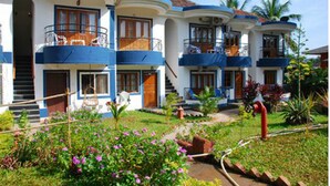 Um edifício com várias andares, varandas, um jardim com flores e um céu claro.