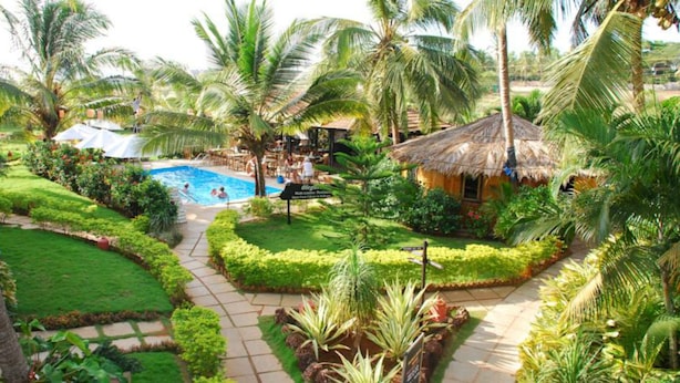 Um resort tropical com piscina, palmeiras e uma cabana de telhado de palha.