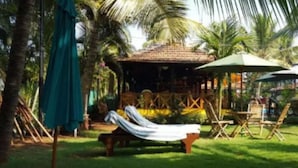 Área de descanso com poltrona, mesinha e um gazebo em um jardim tropical.