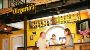 Uma área de bar com uma placa que diz "Olegario's" e um balcão com algumas pessoas sentadas.