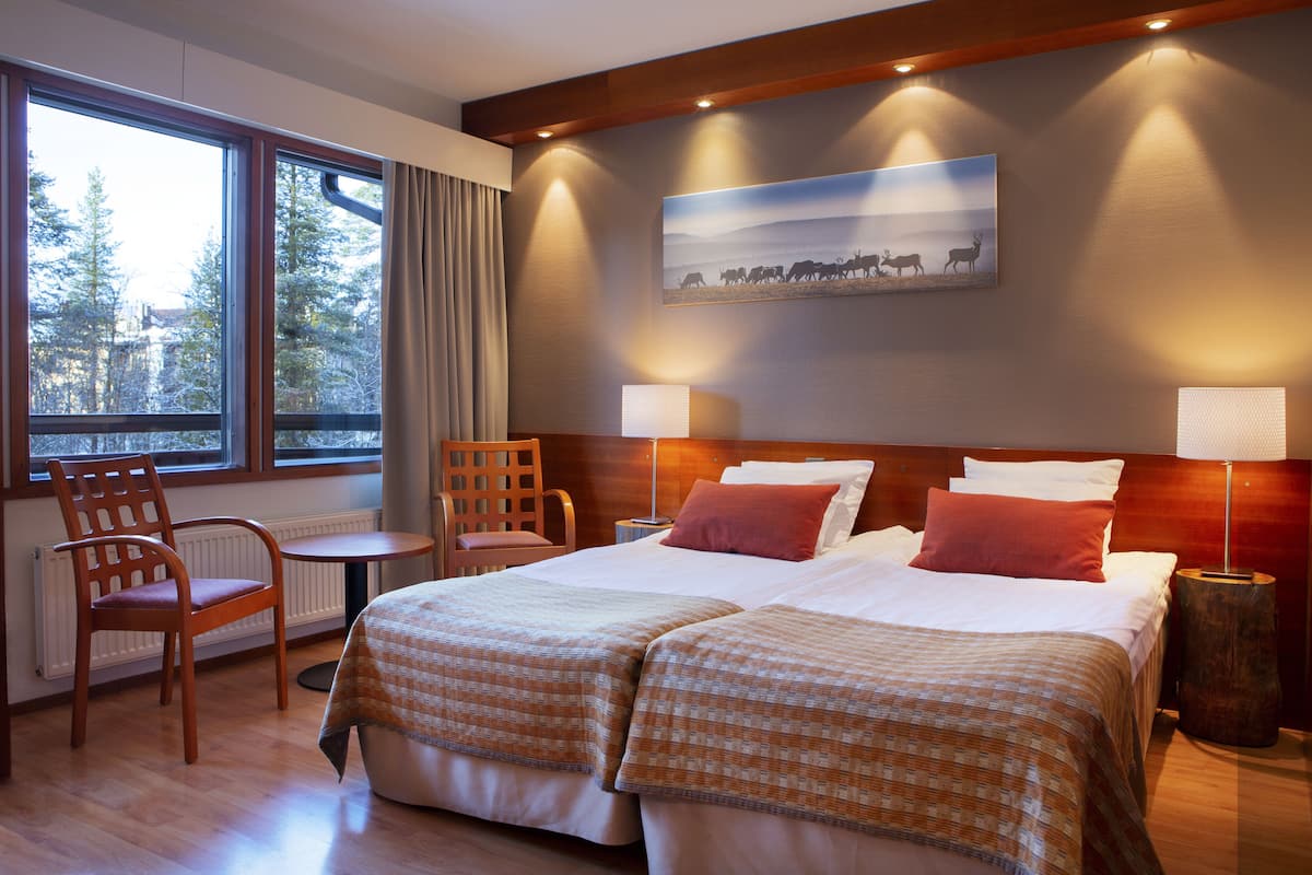 Quarto de hotel com uma cama grande, uma cadeira, uma mesinha e um quadro na parede.