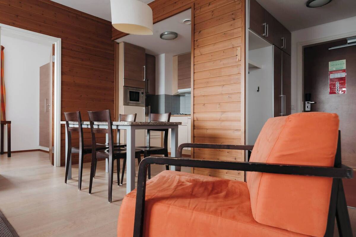 Um interior moderno com um sofá, mesa de jantar, cadeiras e uma poltrona laranja vibrante.