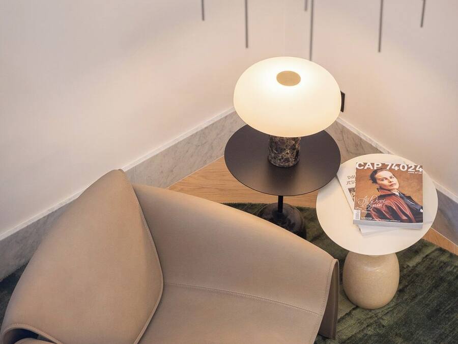 Uma sala de estar moderna com um sofá bege, uma mesa lateral redonda com abajur e uma revista.