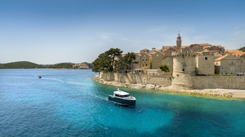 Uma vila costeira com edifícios históricos, mar azul e um barco na água.