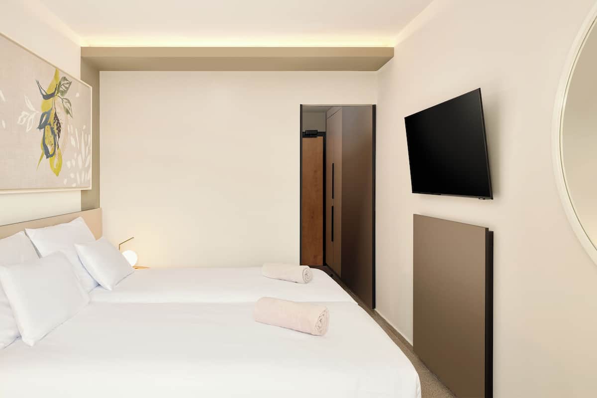 Quarto de hotel com cama, almofadas, televisão de tela plana e um quadro na parede.