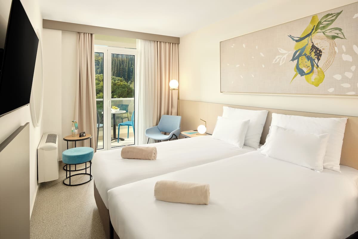 Quarto de hotel com duas camas, televisão, escrivaninha com cadeira e varanda com mesa e cadeiras.
