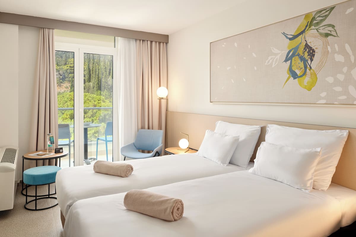 Quarto de hotel com duas camas, uma escrivaninha, uma cadeira e uma janela com cortinas.