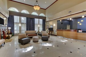 Um hall amplo com balcão de recepção, assentos confortáveis, janelas grandes e um lustre.