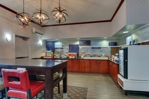 Espaço de café da manhã de hotel com balcão de madeira, uma cadeira vermelha e um candelabro.