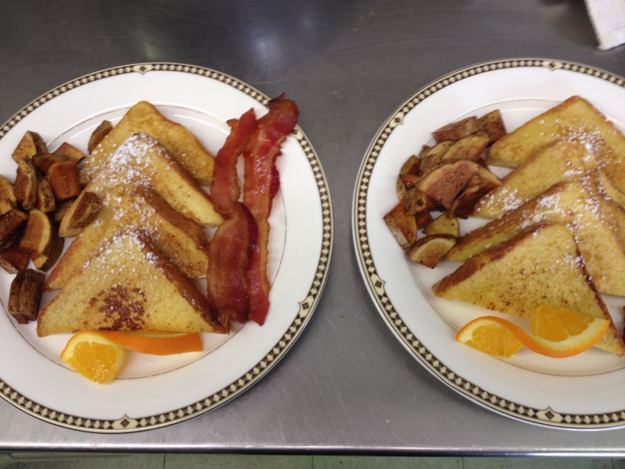 Duas porções de café da manhã com torradas, bacon, batatas e fatias de laranja.