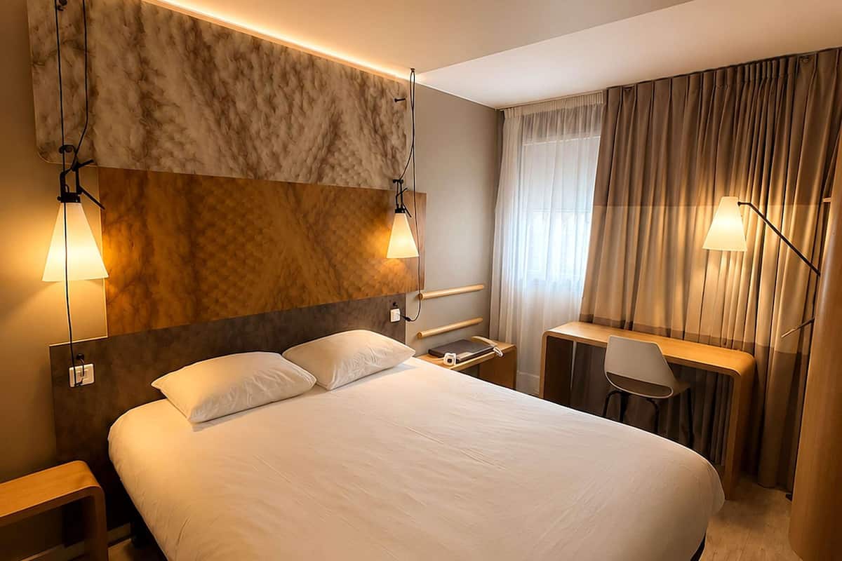 Quarto de hotel com uma cama grande, mesas de cabeceira, uma escrivaninha e uma cadeira.