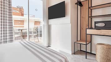 Quarto de hotel moderno com cama grande, televisão fixada na parede, prateleira de madeira e varanda com mesa e cadeiras.
