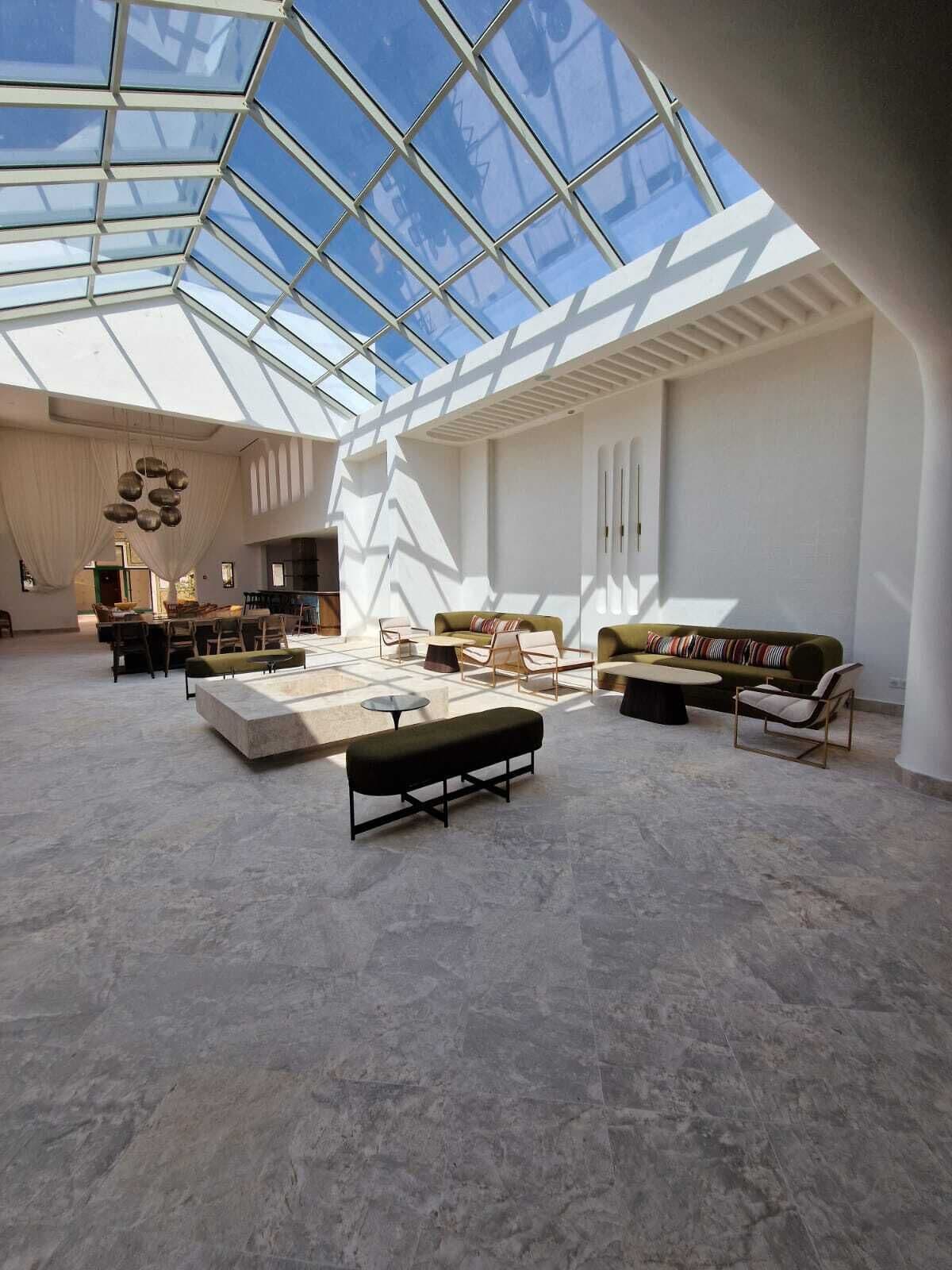 Uma sala de estar ampla com teto alto e claraboia, com um sofá moderno, um banco e um espaço para refeições.