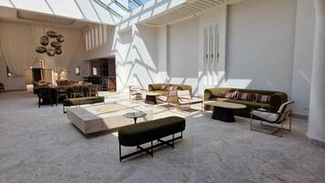 Uma sala de estar ampla com teto alto e claraboia, com um sofá moderno, um banco e um espaço para refeições.