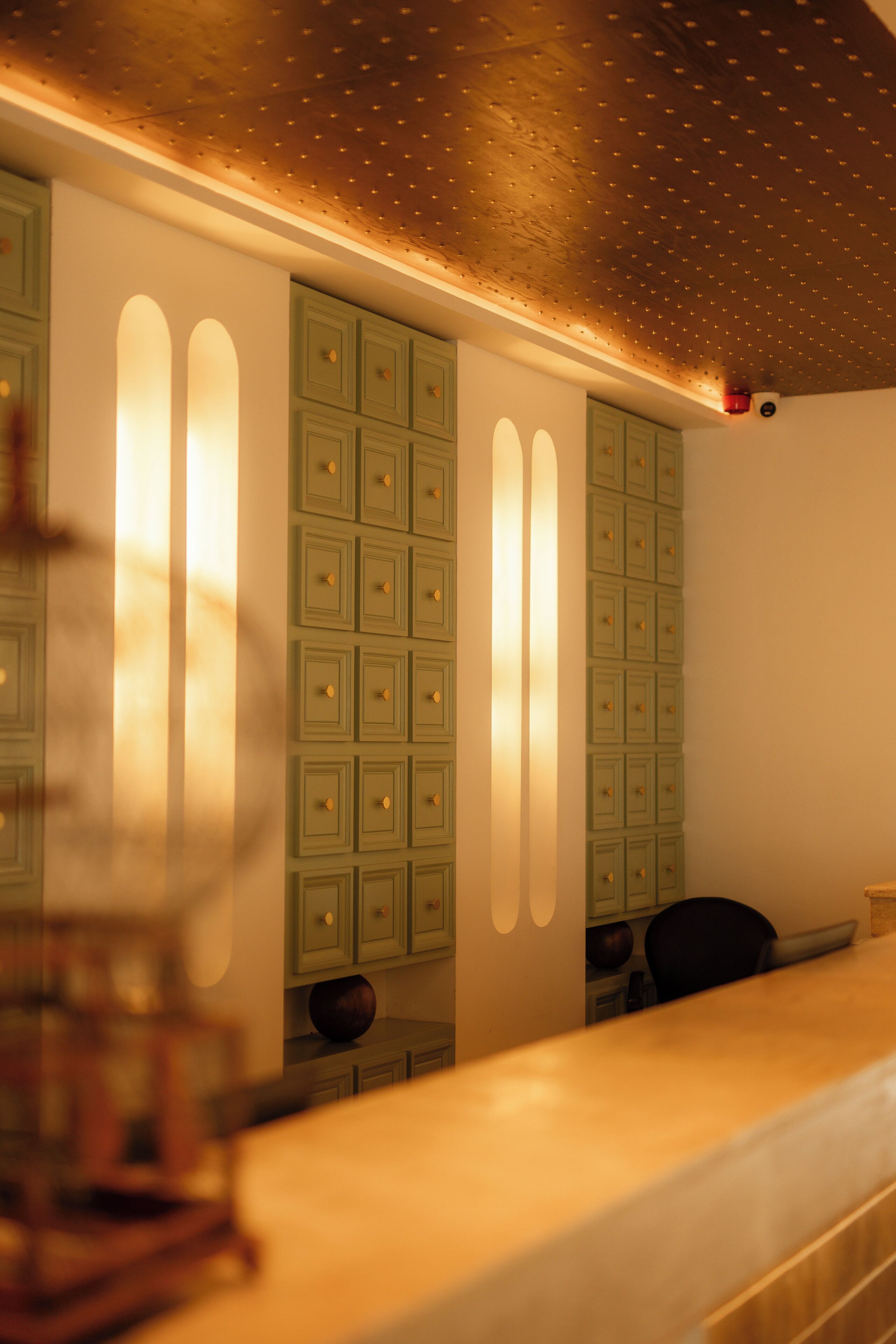 Quarto com teto de madeira, armários verdes com puxadores e parede branca com luminária.