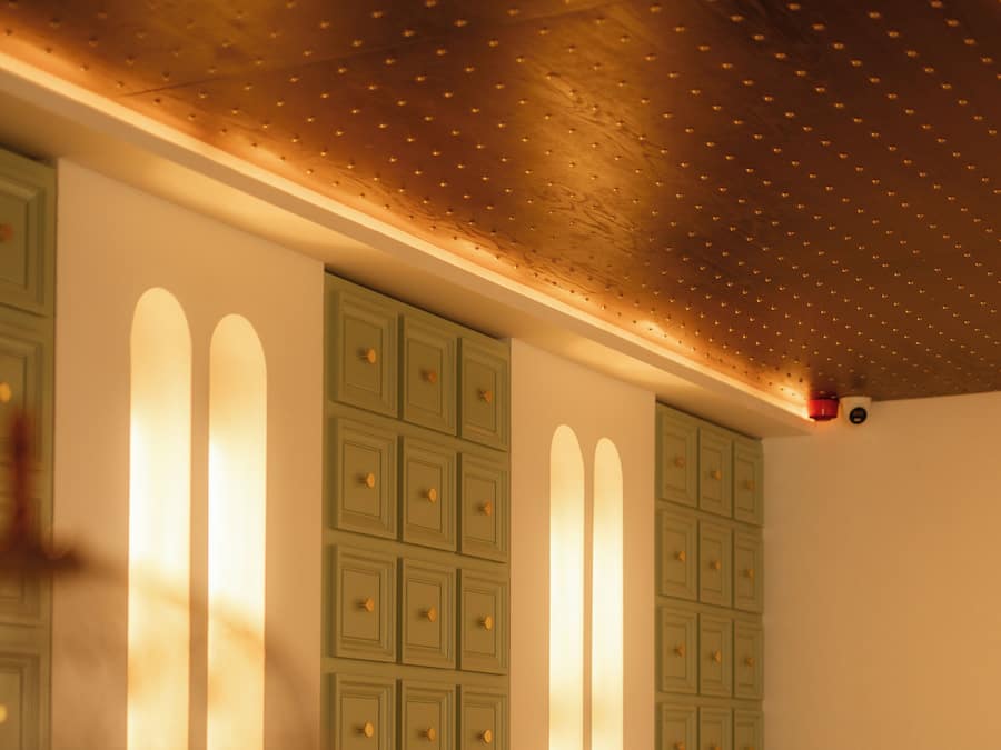 Quarto com teto de madeira, armários verdes com puxadores e parede branca com luminária.